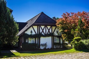 Uma casa tradicional de enxaimel com telhado inclinado, cercada por um jardim bem cuidado e um caminho de pedras.