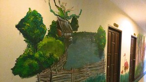 Um mural com uma árvore, uma cerca e um edifício numa parede.