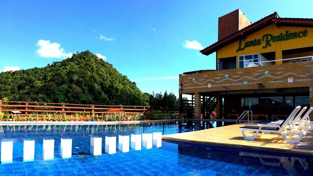 Piscina com espreguiçadeiras, um deck de madeira e o prédio com a inscrição "Lanta Residence" ao fundo.
