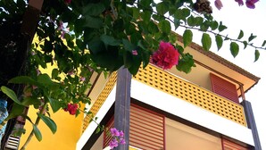 Um edifício de dois andares com fachada amarela, varanda com grade de treliça e placa com a inscrição 