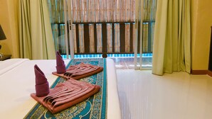 Quarto de hotel com uma cama, uma janela com cortinas de bambu e vista para uma piscina.