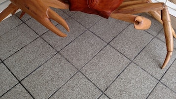 Uma escultura de madeira que se assemelha a um caranguejo, com uma sacola castanha colocada em cima, sobre um chão de azulejos e com um corrimão de metal ao fundo.