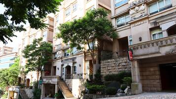 Um edifício de vários andares com fachada de pedra, entrada visível e escadaria que leva ao andar térreo.