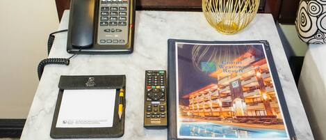 Quarto de hotel com mesa de cabeceira de mármore que acomoda um telefone, um controle remoto, um tablet e um abajur decorativo.