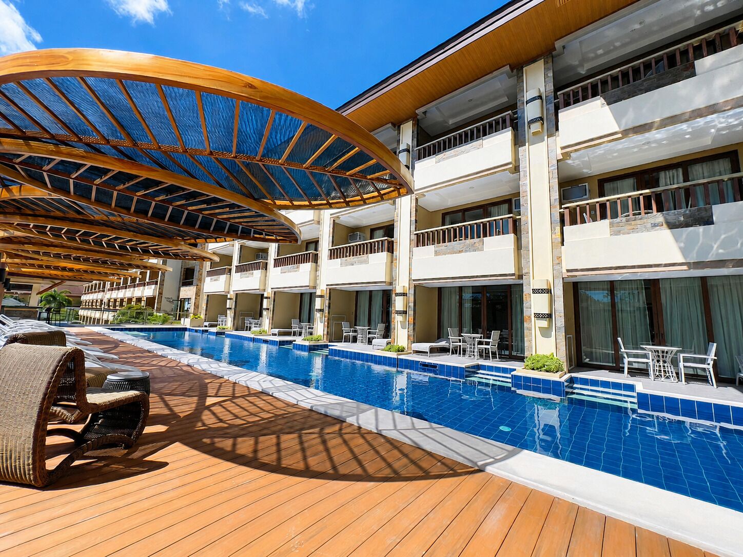 Um hotel com vários andares, piscina, área de estar externa e um deque coberto.