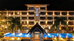 Hotel com piscina, várias varandas e entrada central com estrutura de telhado peculiar.