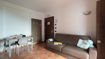 Uma sala de estar com um sofá, uma mesa de jantar com cadeiras e uma porta com um letreiro.