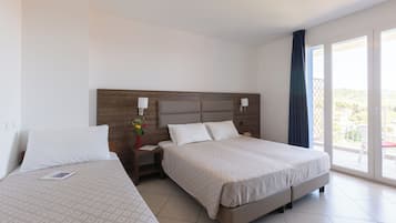 Quarto de hotel com duas camas, uma mesa de cabeceira com abajur e vista para o exterior.