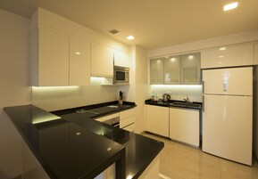 Uma cozinha moderna com armários brancos, bancada preta, micro-ondas, frigorífico e pia.