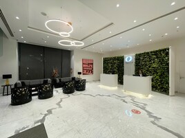 Uma área de recepção moderna, com piso de mármore, assentos estofados em preto e um painel vertical com jardim.
