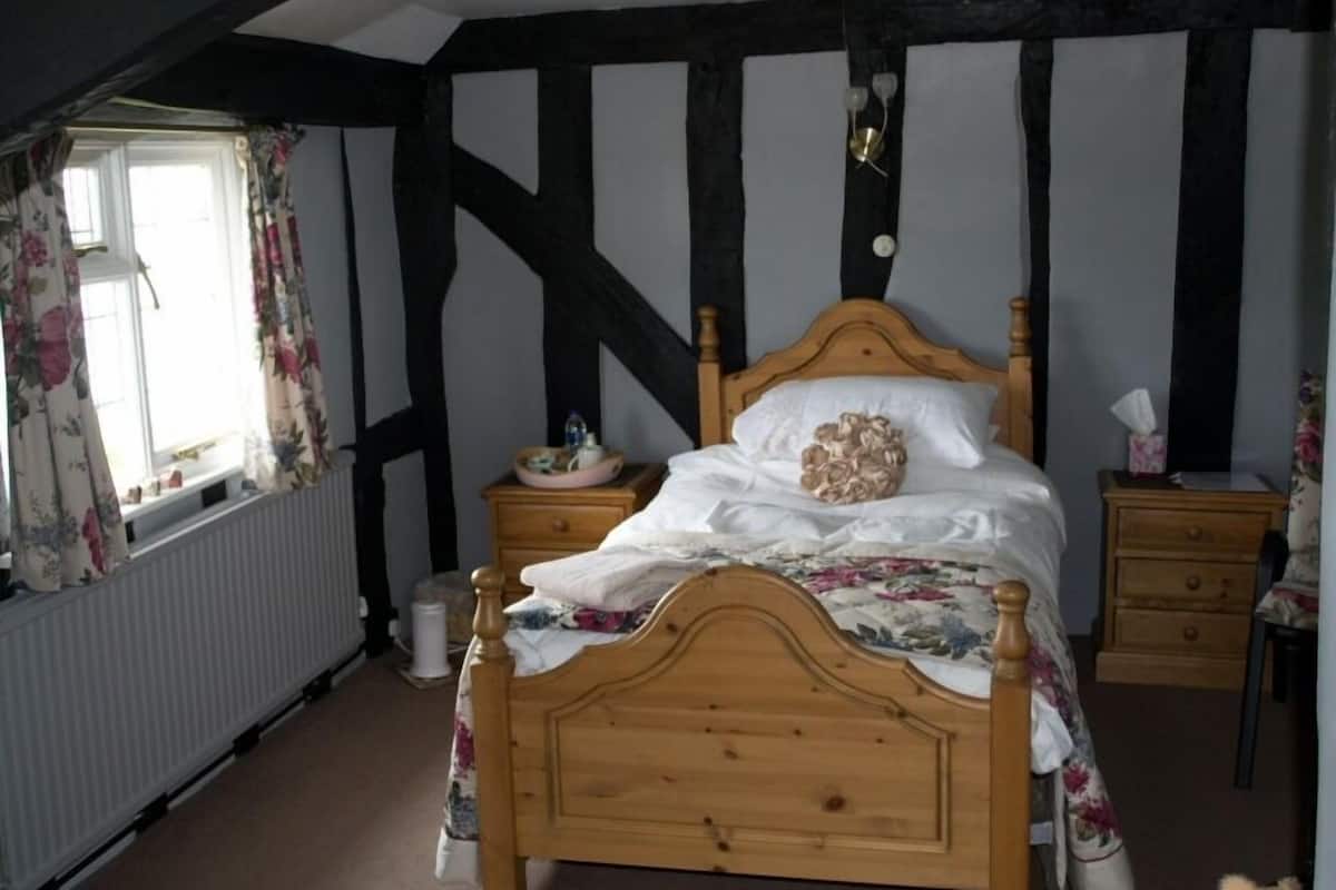 Quarto com cama de madeira, mesa de cabeceira, cômoda e janela com cortinas florais.