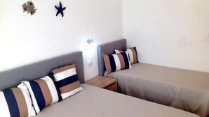 Duas camas de solteiro com almofadas listradas, um criado-mudo pequeno e um adorno de estrela fixado na parede.