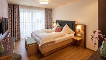 Quarto moderno com cama de madeira, mesas de cabeceira com luminárias, um banquinho no pé da cama e uma TV na parede à esquerda.