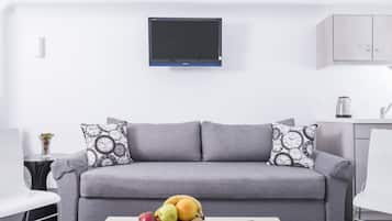 Uma sala de estar moderna com um sofá cinza, almofadas estampadas, uma fruteira, televisão na parede e design minimalista.