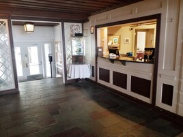 Um hall de hotel com balcão de recepção, geladeira, mesa com toalha branca e vista para a área da cozinha.