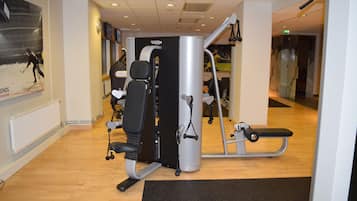 Uma academia com equipamentos de exercícios, um pôster na parede e piso de madeira.
