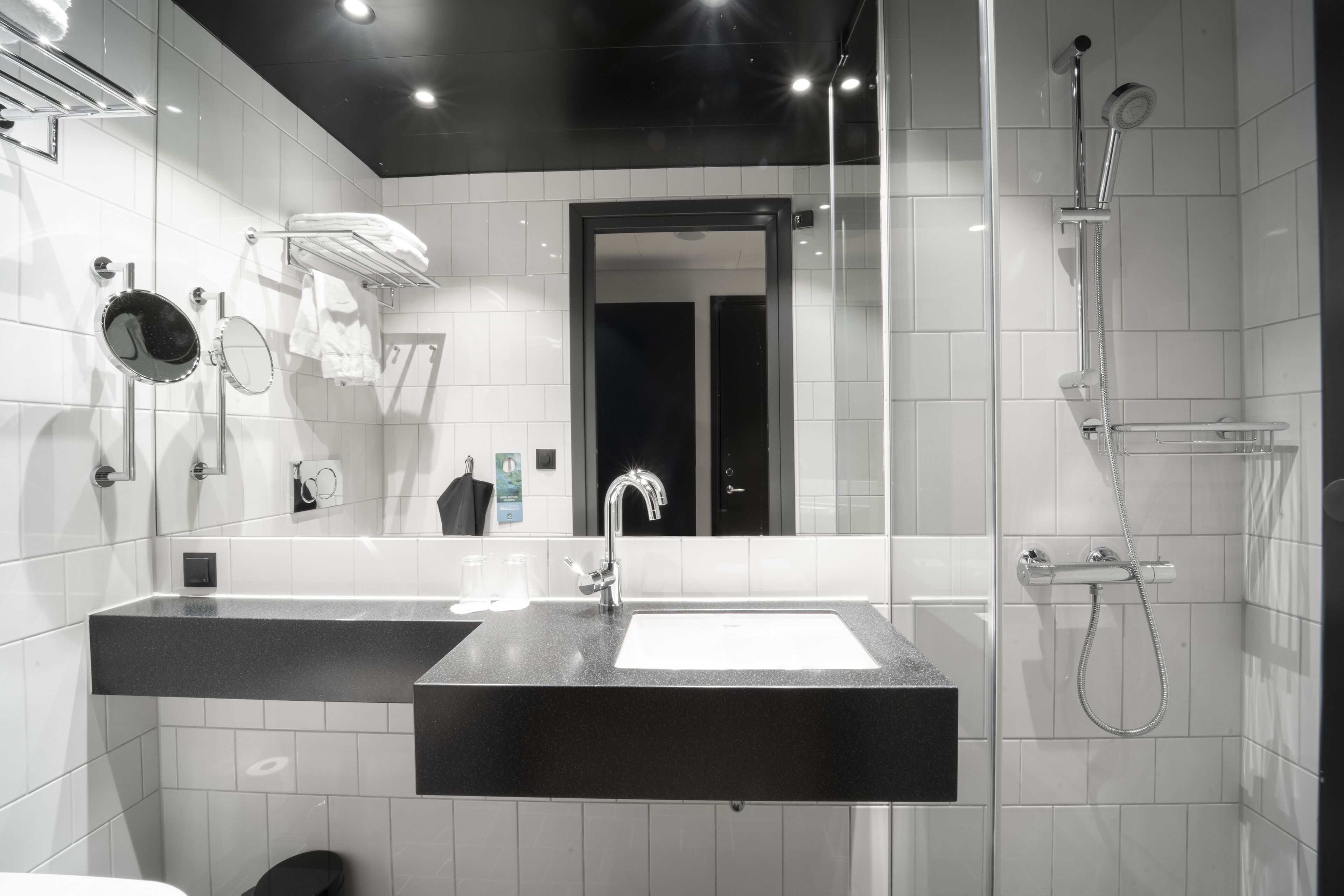 Uma casa de banho moderna com uma pia preta, um espelho e um chuveiro.