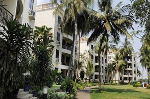 Hotel de vários andares com varandas, cercado por vegetação exuberante e palmeiras.