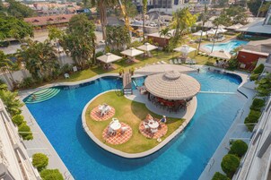 Uma piscina grande com várias áreas, rodeada por palmeiras e zonas de estar ao ar livre.