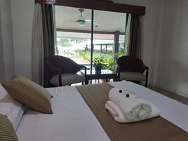 Quarto de hotel com uma cama, duas cadeiras, uma mesa com uma planta e vista para a área externa.