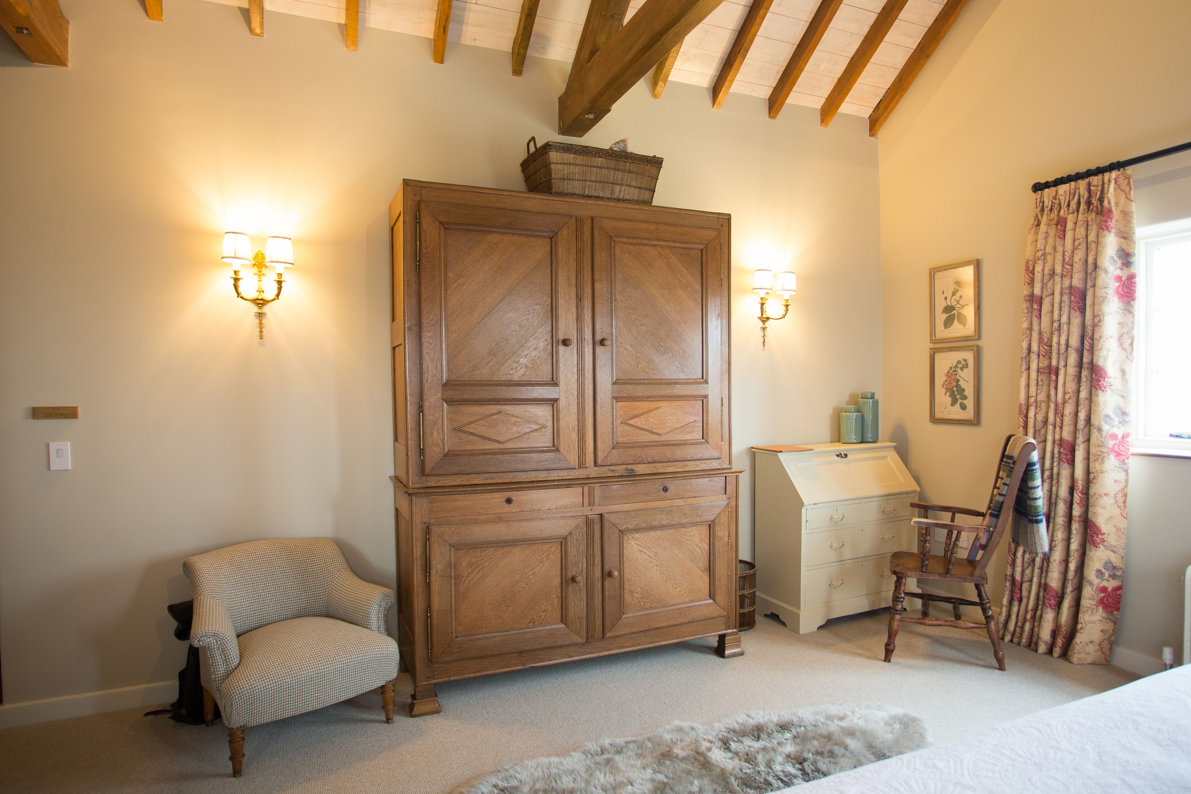 Quarto com armário de madeira, uma cadeira, escrivaninha e janela com cortinas.