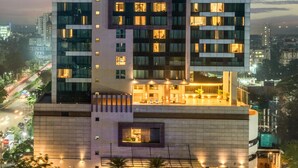 Um hotel moderno com uma placa chamativa, vários andares e vista para a paisagem urbana ao redor.