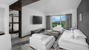 Quarto de hotel moderno com uma janela ampla, televisão de tela plana, sofá, mesa de centro e cama com cabeceira.