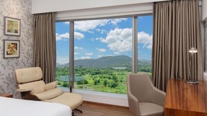 Quarto de hotel com uma grande janela, duas cadeiras, uma cama e uma mesa.