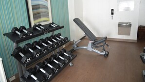 Centro de ginástica com halteres, um banco e uma placa fixada na parede.
