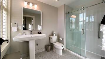 Uma casa de banho moderna com lavatório branco, espelho e sanita, e área de duche com divisória de vidro.