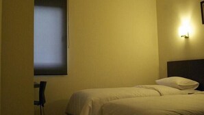 Quarto de hotel com duas camas, uma cadeira e luminária fixada na parede.