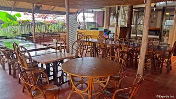 Restaurante com mesas e cadeiras de madeira, um balcão e vista para o jardim.
