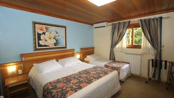 Quarto de hotel com duas camas, cabeceiras de madeira, mesa de cabeceira e uma janela com cortinas, além de um ar condicionado.