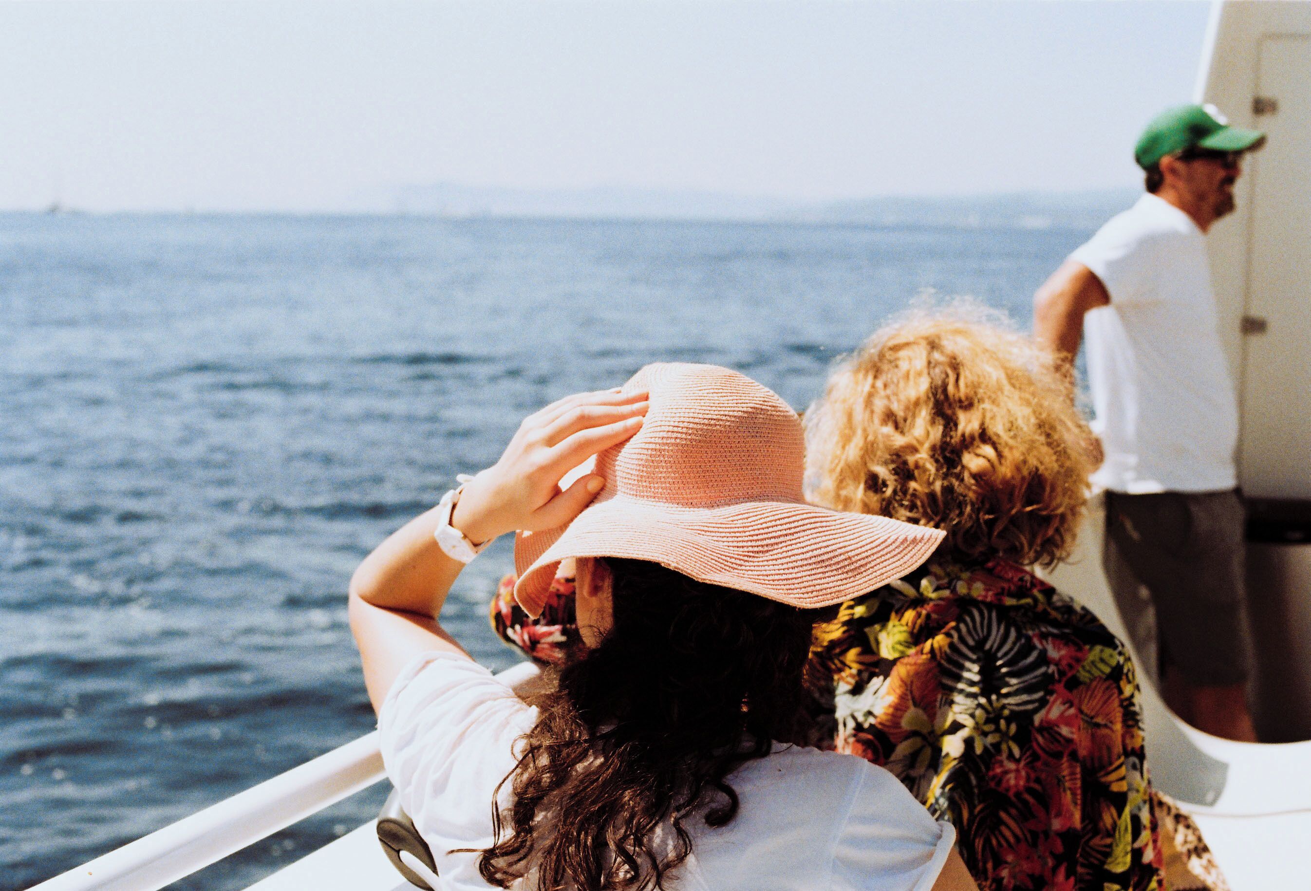 Um barco com duas pessoas usando chapéus, uma de camisa branca e outra de camisa florida, com vista para o mar.
