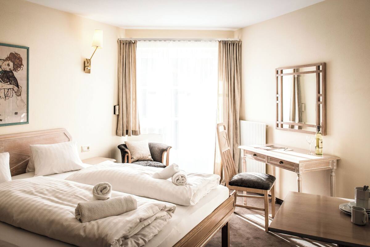Quarto de hotel com uma cama, uma escrivaninha, uma cadeira, um espelho e um quadro na parede.