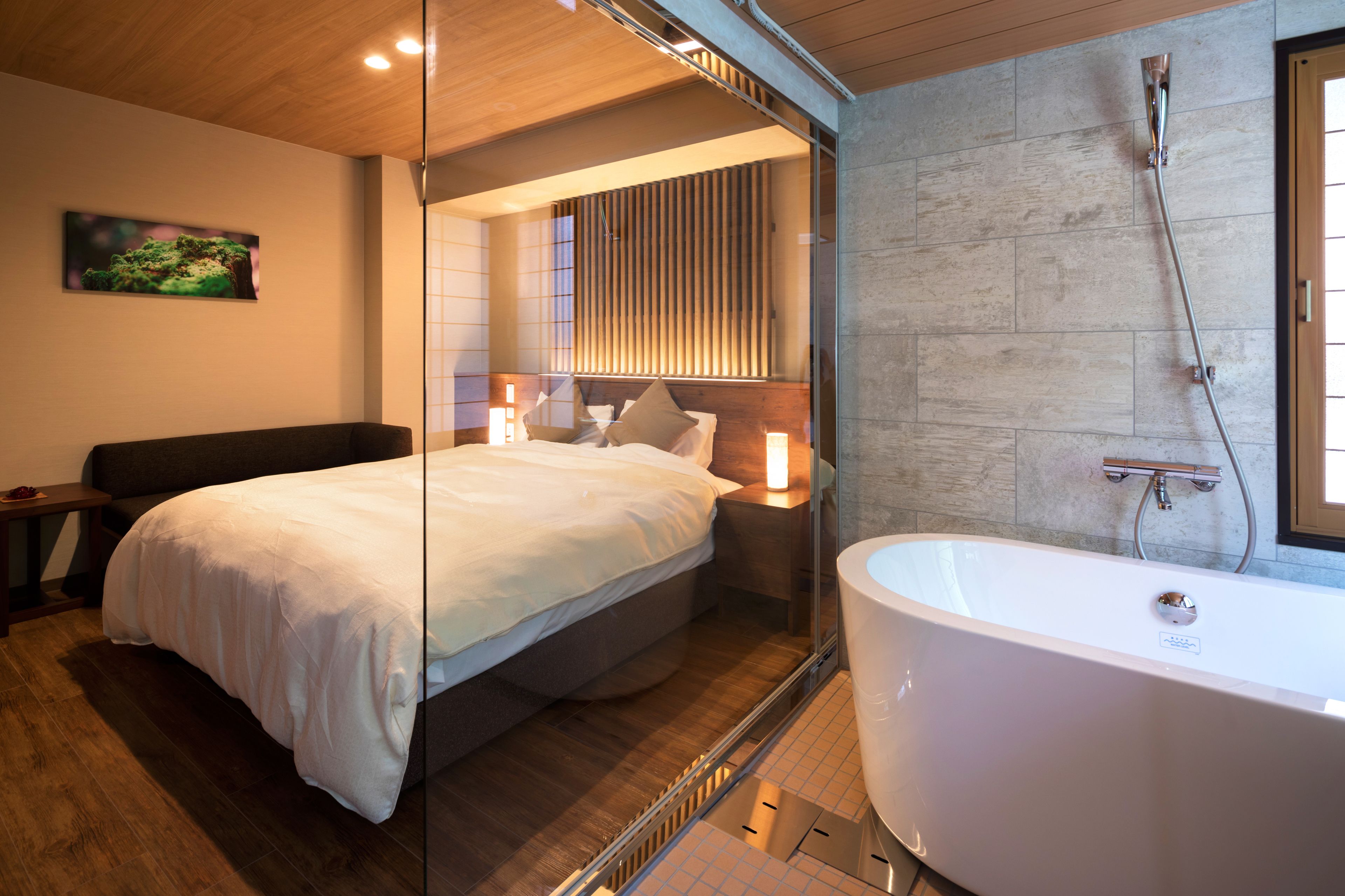 Quarto moderno com uma cama grande, chuveiro com box de vidro e vista para a cidade.