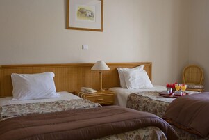 Quarto de hotel com duas camas, uma mesinha de cabeceira com abajur, um quadro na parede e uma pequena mesa com itens de café da manhã.