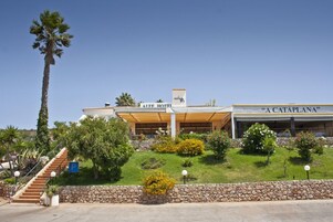 Hotel com área externa coberta, parede de pedra e uma palmeira.