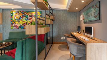 Uma sala de estar moderna com um sofá verde, uma escrivaninha de madeira com um computador e um quadro abstrato colorido na parede.