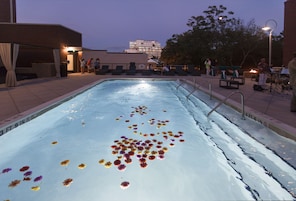Piscina com borda transparente e área rasa, rodeada por espreguiçadeiras e uma área coberta.