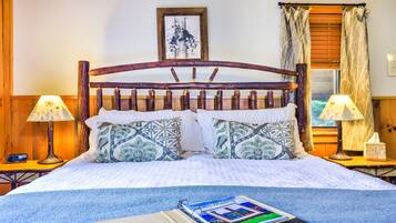 Uma cama bem arrumada com almofadas estampadas, cabeceira de madeira e mesa de cabeceira com abajur e um livro.