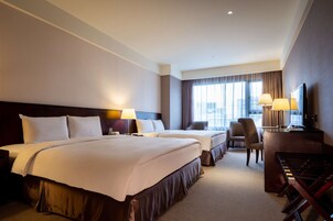 Quarto de hotel com duas camas, uma escrivaninha, uma cadeira e uma televisão.