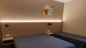 Quarto de hotel com duas camas, uma luminária na parede e uma mesa pequena.