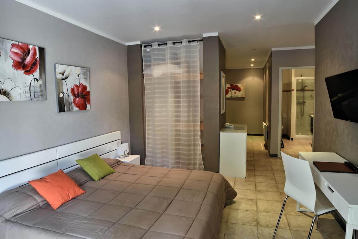 Quarto moderno com cama, escrivaninha e zona de chuveiro.