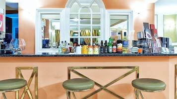 Uma área de bar com máquina de café, diversas garrafas e uma janela com cortinas. Há três bancos com assentos verdes.