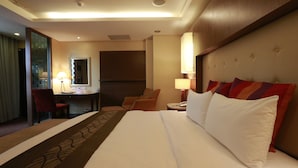 Quarto de hotel com uma cama grande, uma escrivaninha com cadeira, um espelho e uma televisão.