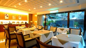 Um restaurante com várias mesas e cadeiras, um balcão com uma máquina de café e vista para o exterior através de grandes janelas.