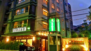 Hotel com vários andares, letreiros iluminados e um carro estacionado em frente.