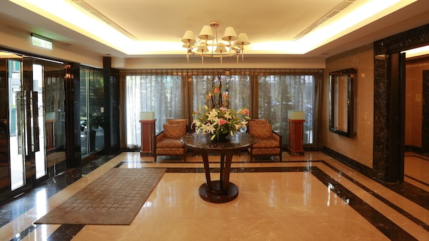 Um hall com piso de mármore, uma mesa redonda com um vaso de flores, duas poltronas, um candelabro e um espelho grande.