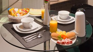 Uma mesa de vidro com arrumação de café da manhã, uma banheira de hidromassagem e um banheiro com paredes verde-água e pia branca.